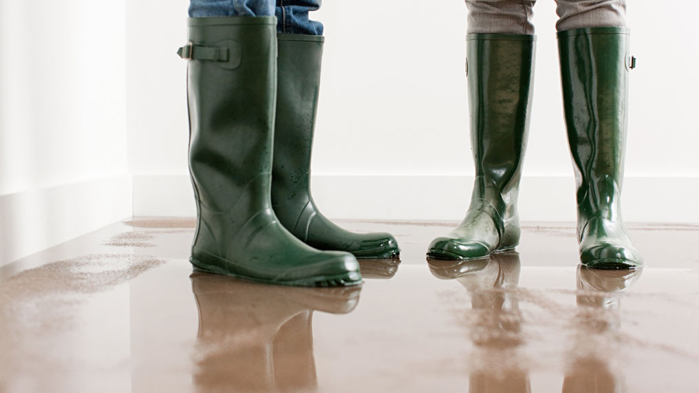 Two people wear wellington boots while stood in a flooded house.